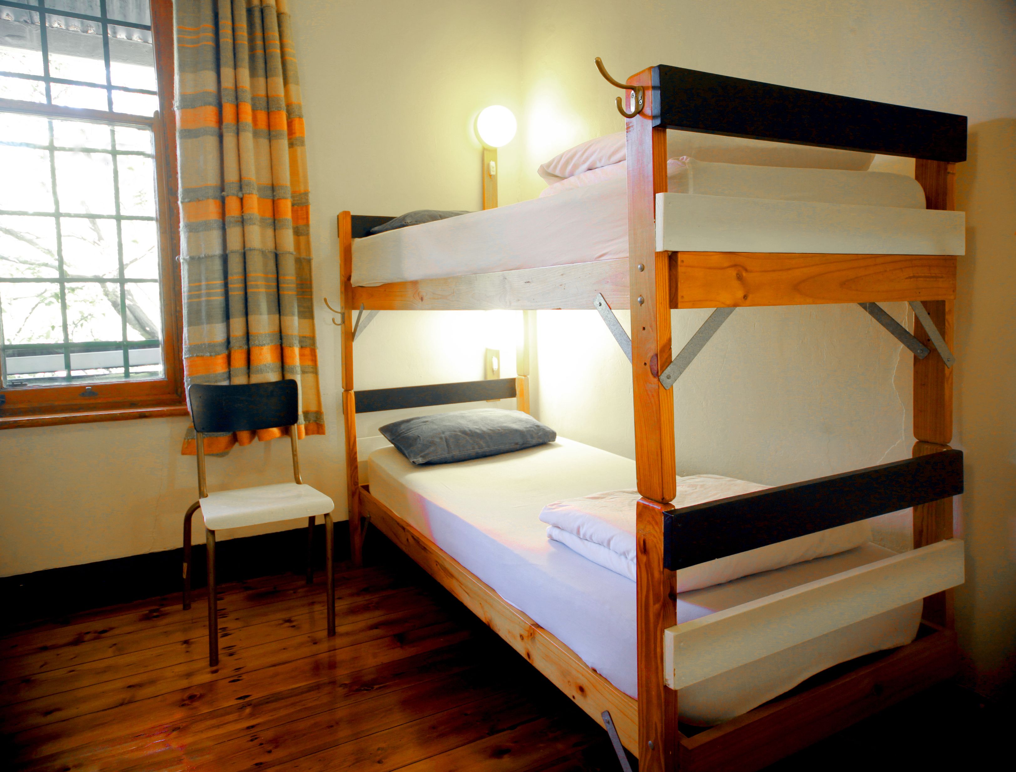 Uma cama beliche com estrutura de madeira, uma cama de solteiro embaixo e uma cadeira.