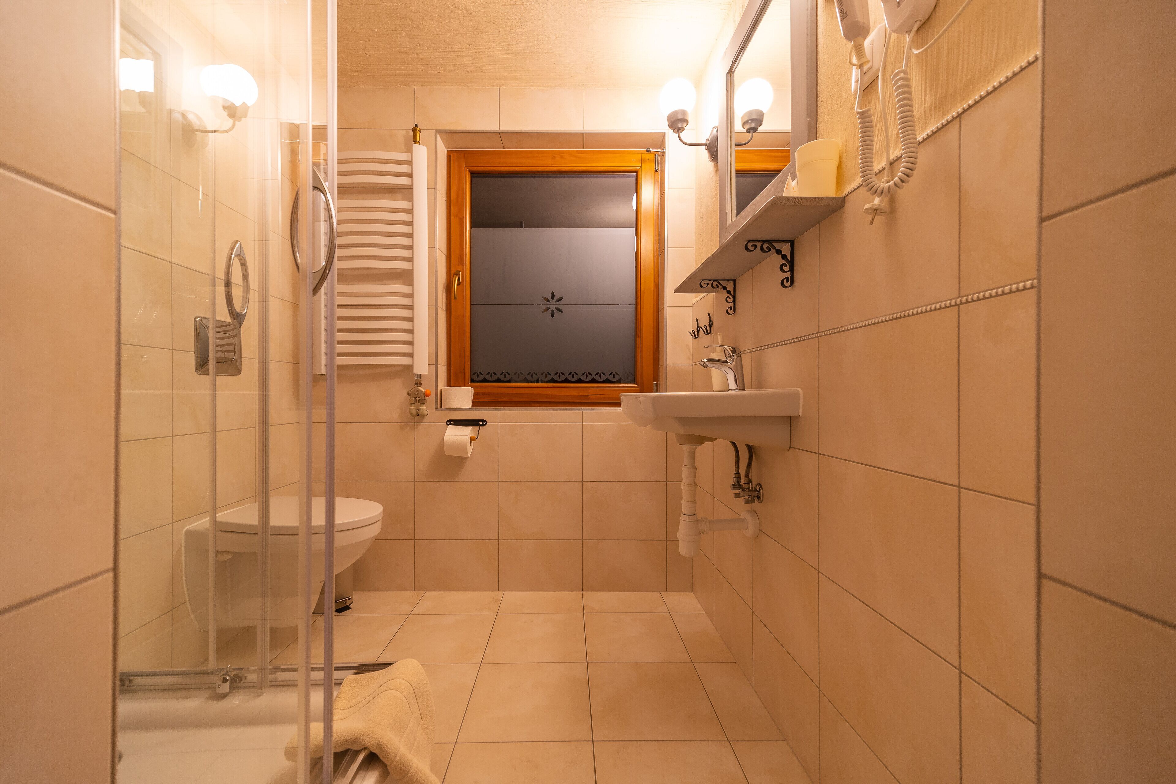 Uma casa de banho pequena, com azulejos, com sanita, lavatório e chuveiro.