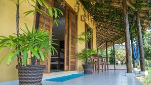 Uma área externa coberta com plantas em vasos, móveis de madeira e piso de azulejos.