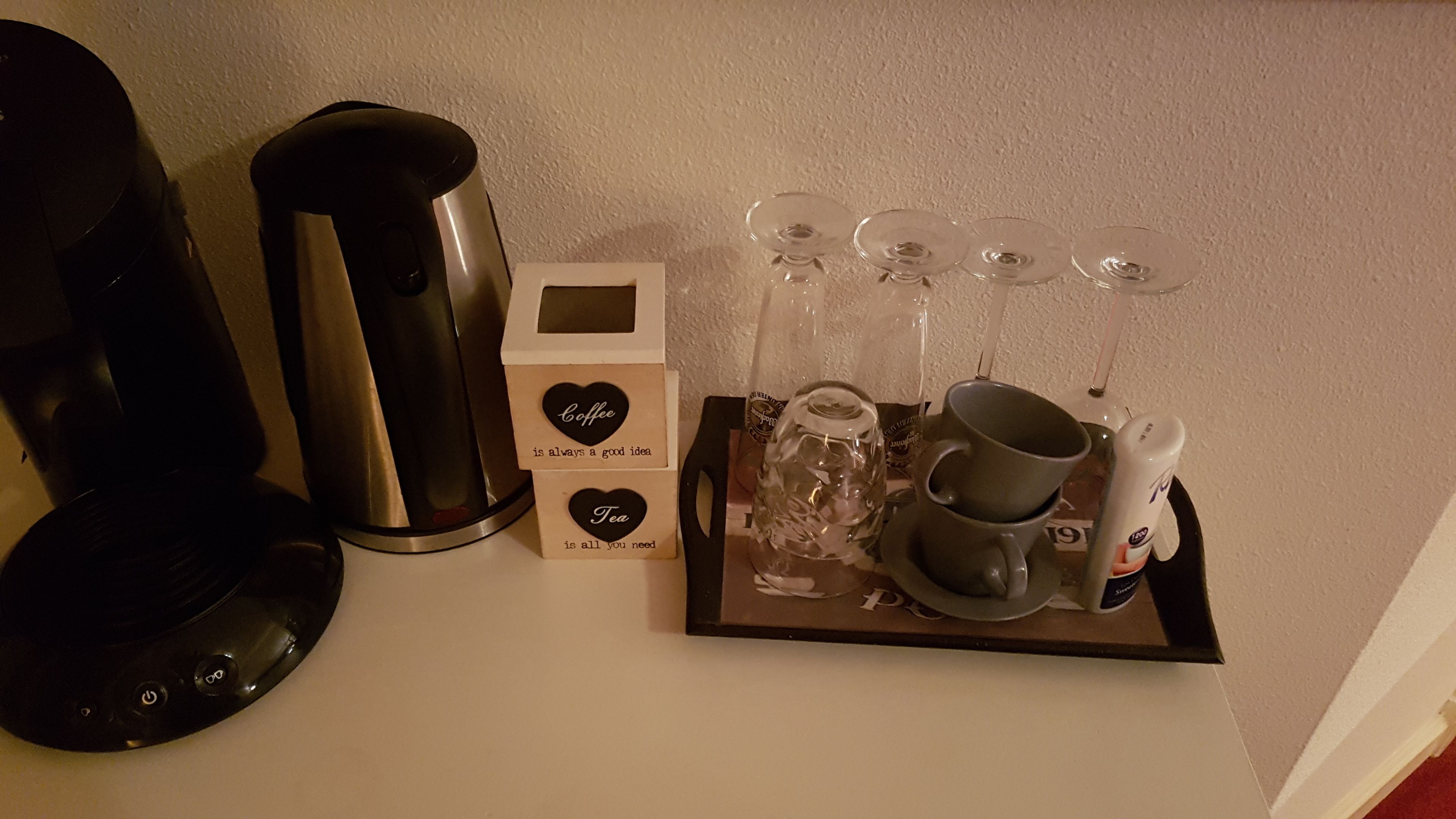 Cantinho de café e chá com cafeteira, caixa de chá, copos e xícaras.