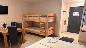 Uma cama beliche com escrivaninha e cadeiras, uma cama de solteiro com cobertor, e uma porta com placa.
