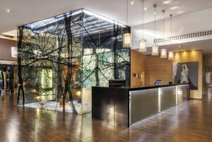 Uma área de recepção moderna com divisória de vidro com design de árvore, balcão de atendimento e iluminação pendente.