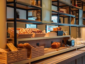 Uma vitrine de padaria com diversos produtos de panificação, caixas de madeira e prateleiras.