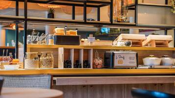 Um balcão de café da manhã com diversos alimentos, uma máquina de café e uma placa indicando opções de café e chá.