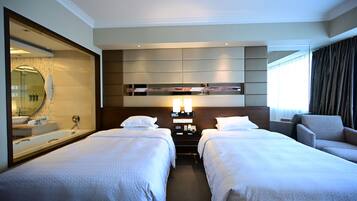 Quarto de hotel com duas camas, um espelho grande, banheiro com banheira e área de estar com sofá.