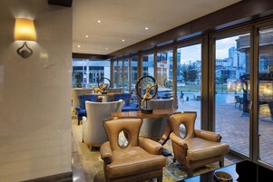 Um lobby moderno com poltronas de couro, um balcão de recepção e grandes janelas com vista para a paisagem urbana.