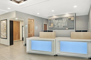 Uma área de recepção com design moderno, destacando-se um balcão de atendimento, um quadro de informações fixado na parede e um corredor que dá acesso a outras áreas.