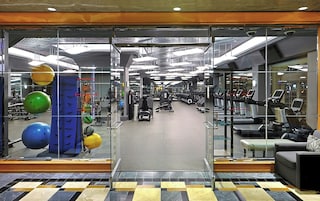 Uma academia com equipamentos de ginástica, um espelho grande e piso xadrez.