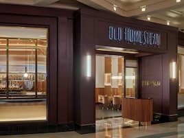 Entrada de hotel com design moderno, destacando uma placa grande para 'Old Homestead Steak House'.