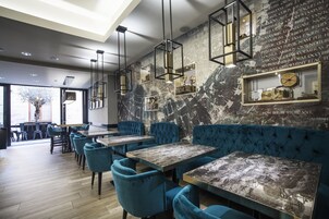 Interior de restaurante moderno com assentos estofados em azul, mesas com tampos de mármore e iluminação pendente.