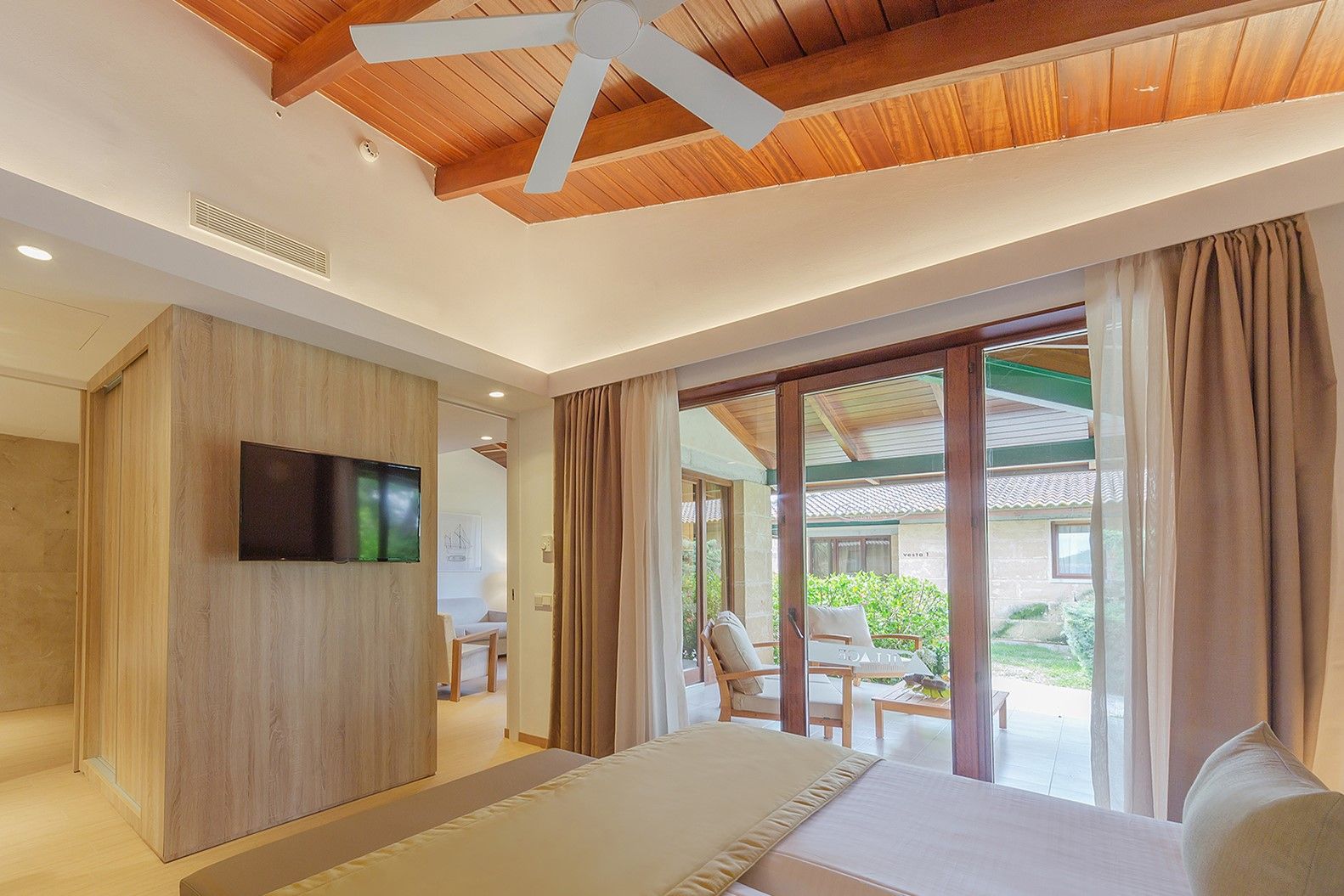 Quarto com cama, televisão, ventoinha no teto e vista para o exterior.
