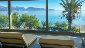 Quarto com amplas janelas que oferecem vista para um corpo de água e montanhas. Várias poltronas de descanso estão em primeiro plano.