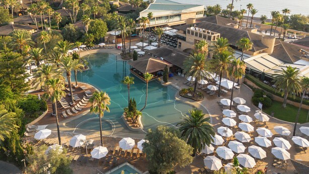 Um resort com uma piscina grande, palmeiras e vista para o oceano.