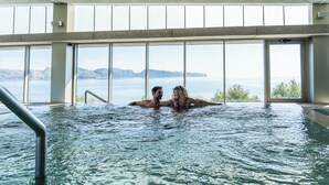 Um casal em uma piscina interna ampla com vista para montanhas através de grandes janelas.