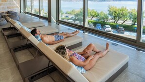 Espaço relaxante iluminado por luz do sol, com várias poltronas e uma grande janela que oferece vista para um estacionamento e montanhas.