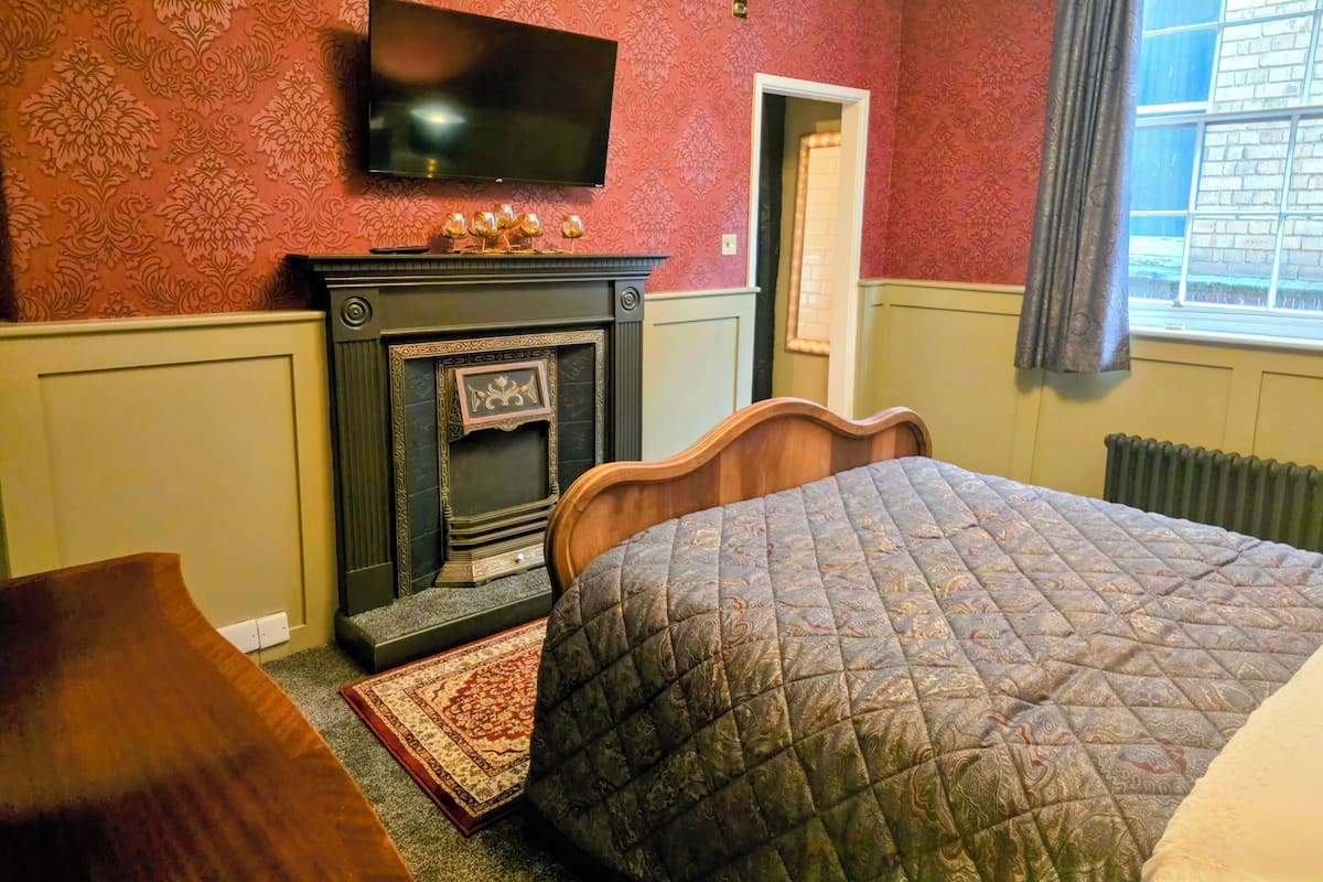 Quarto de hotel com uma cama, televisão sobre a lareira e janela com cortinas.