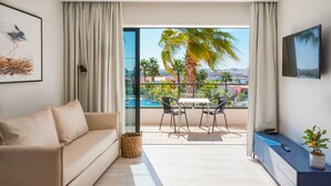 Sala de estar moderna com sofá, área de refeições com cadeiras, televisão e vista para uma piscina e palmeiras.
