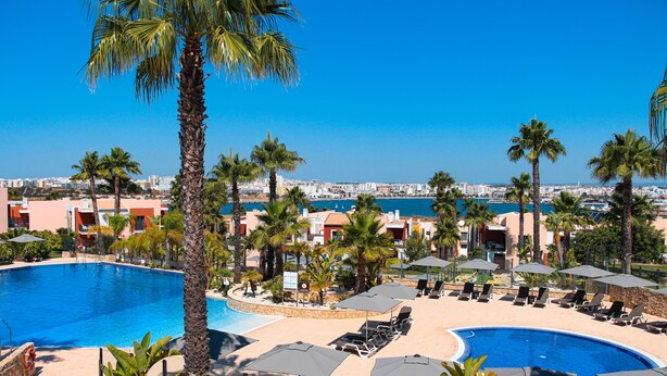 Um resort com uma piscina grande, palmeiras e vista para a cidade.