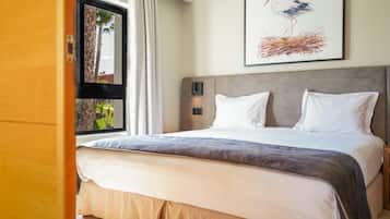 Quarto de hotel com uma cama grande, janela com vista para palmeiras e uma obra de arte emoldurada de uma cegonha e ninho na parede.