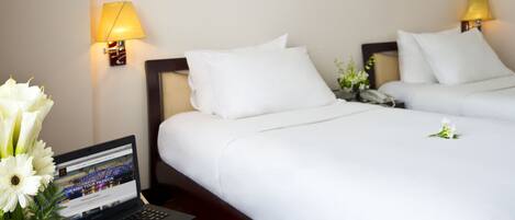 Quarto de hotel com duas camas, um laptop sobre uma mesa de cabeceira e quadros nas paredes.