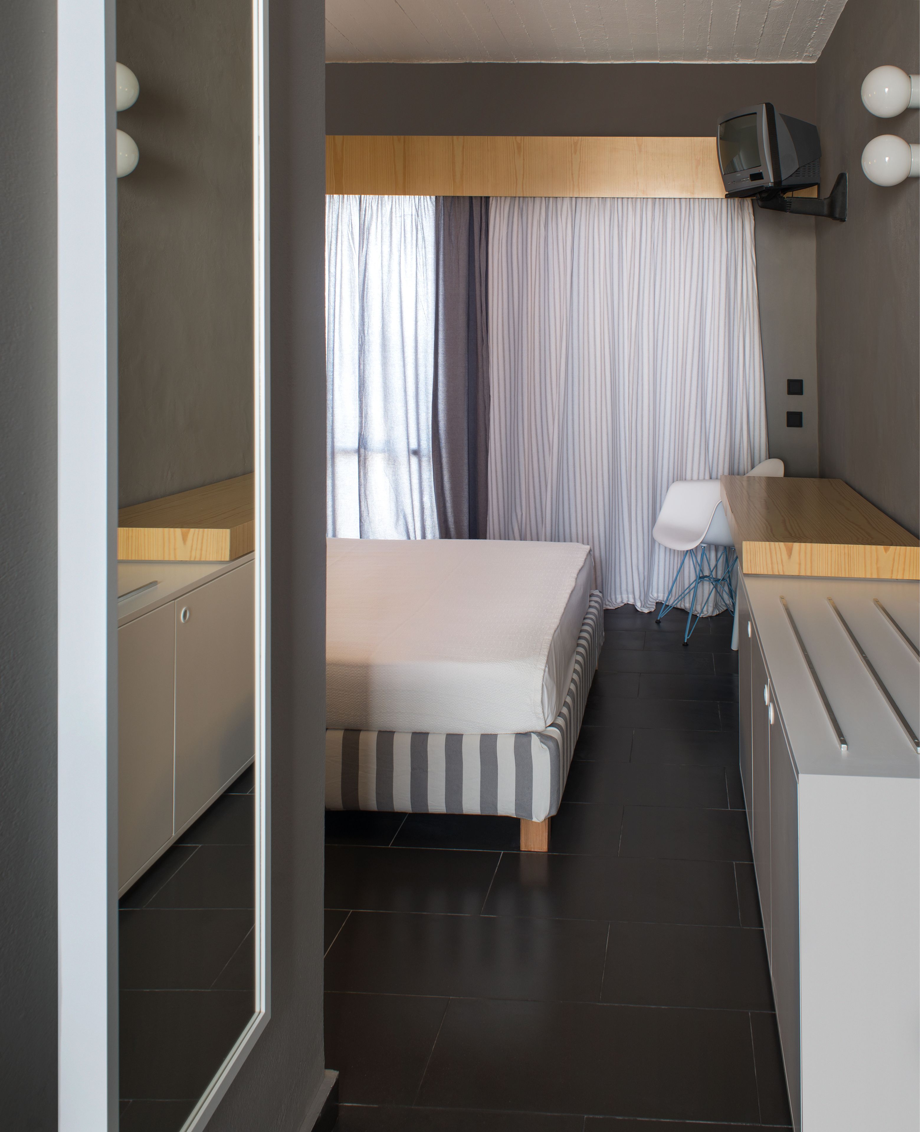 Quarto de hotel pequeno com cama, escrivaninha e televisão.