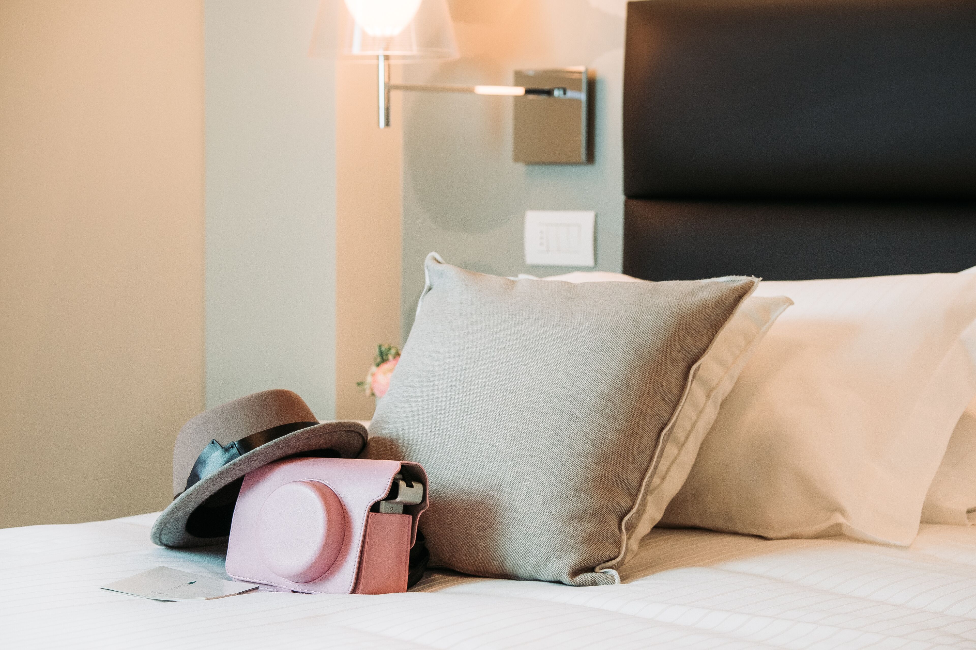 Cama bem arrumada com almofadas, um chapéu e uma bolsa rosa sobre ela.