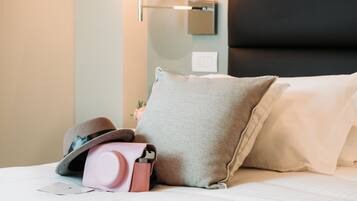 Cama bem arrumada com almofadas, um chapéu e uma bolsa rosa sobre ela.