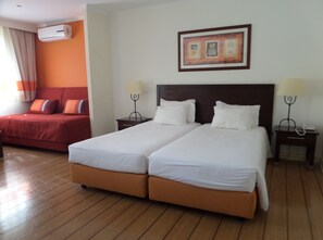 Quarto de hotel com duas camas, um sofá vermelho, um quadro na parede e uma janela com cortinas.