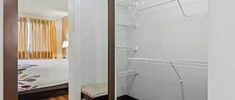 Quarto de hotel com cama, um banco e um closet espaçoso com prateleiras.