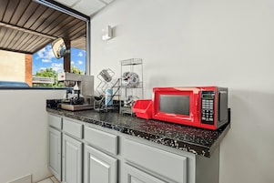 Uma cozinha com um micro-ondas vermelho, uma cafeteira e uma estante de metal com louças.