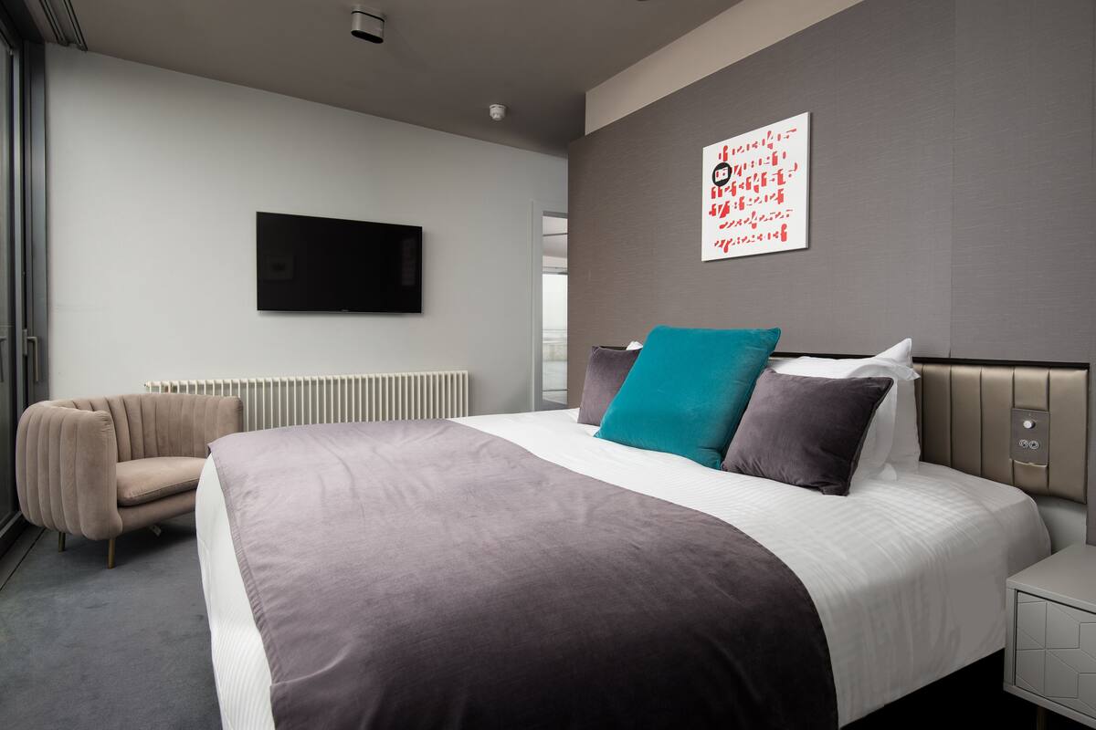 Quarto de hotel moderno com uma cama grande, televisão de tela plana na parede, sofá e radiador.