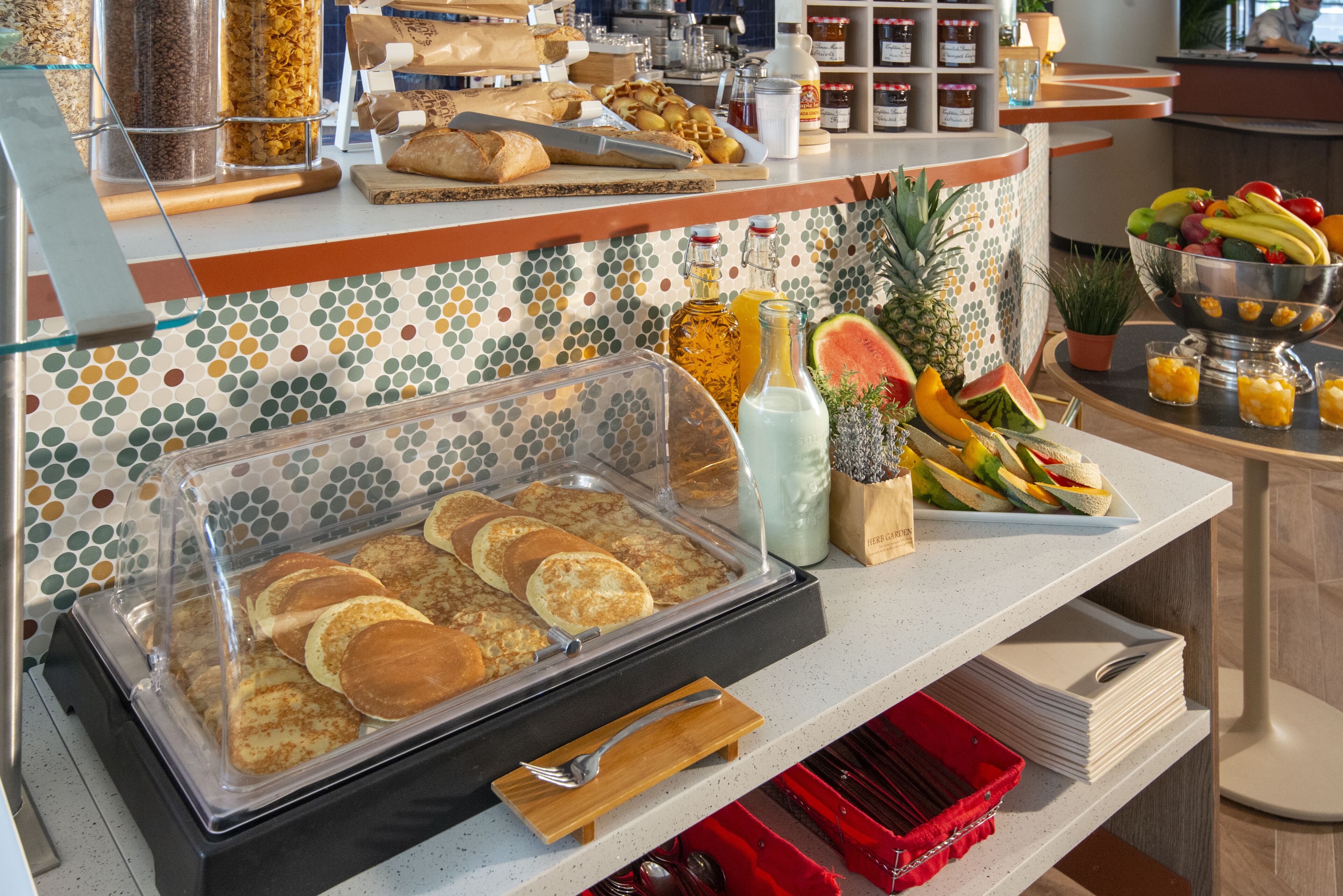 Uma área de buffet com diversas opções de comida, incluindo panquecas, sanduíches e frutas.