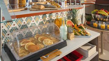 Uma área de buffet com diversas opções de comida, incluindo panquecas, sanduíches e frutas.