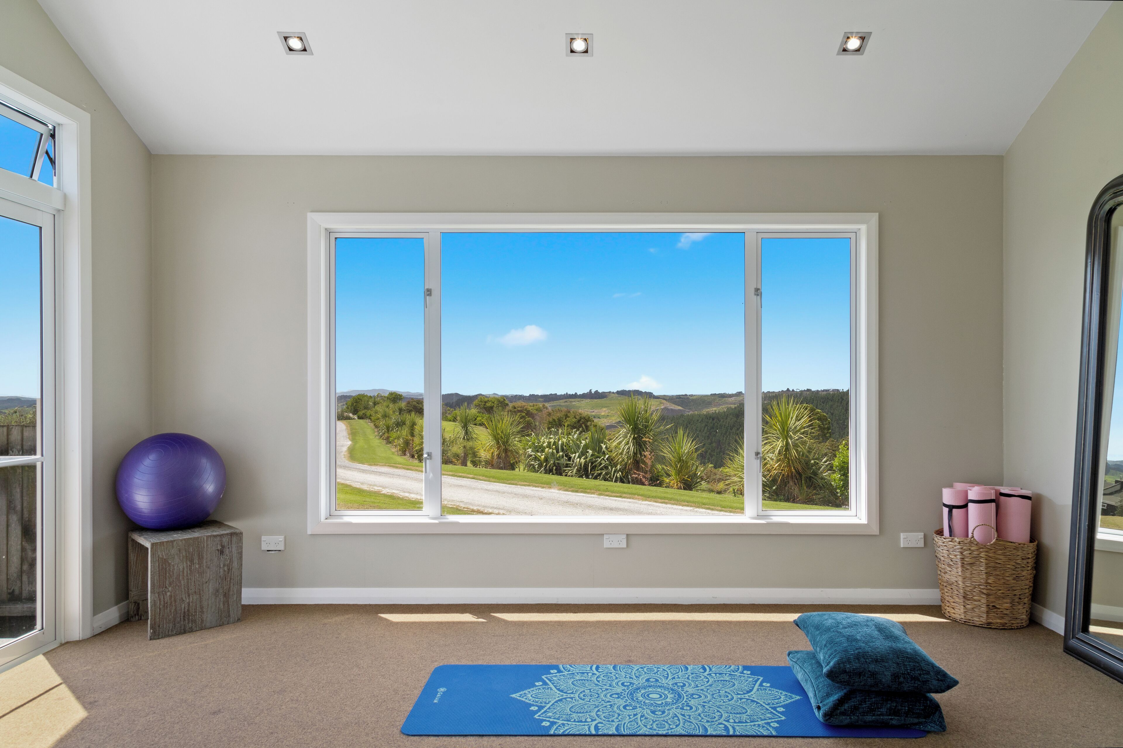 Quarto com uma janela ampla que oferece vista para uma estrada e vegetação, um tapete de yoga, um colchonete de meditação e uma bola de pilates.