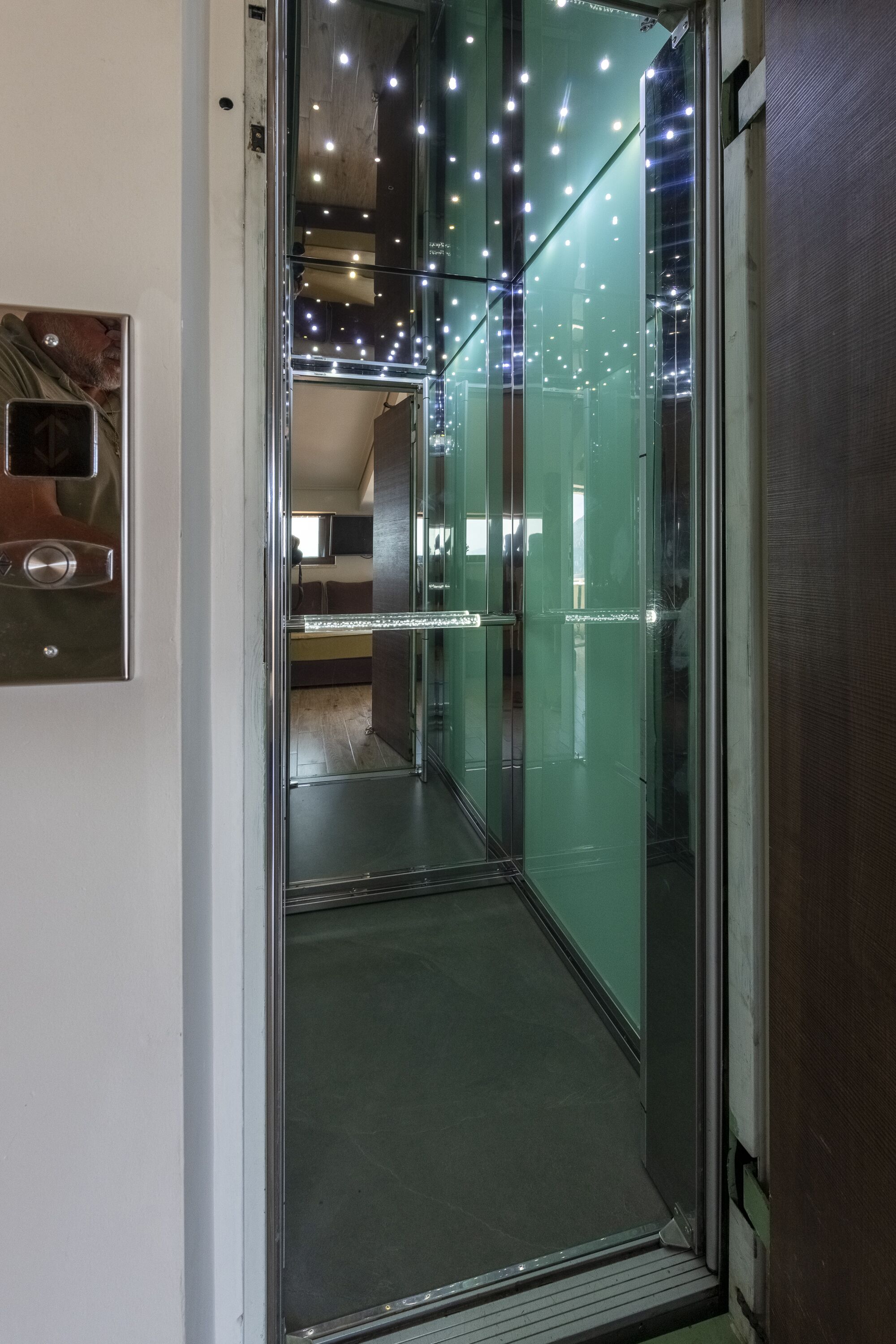 Elevador moderno com portas de vidro, painel de controle visível e interior bem iluminado.