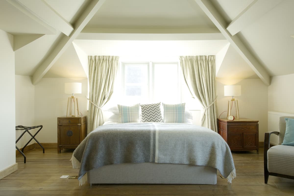 Quarto com cama grande, duas mesas de cabeceira, uma cadeira e janela com cortinas.