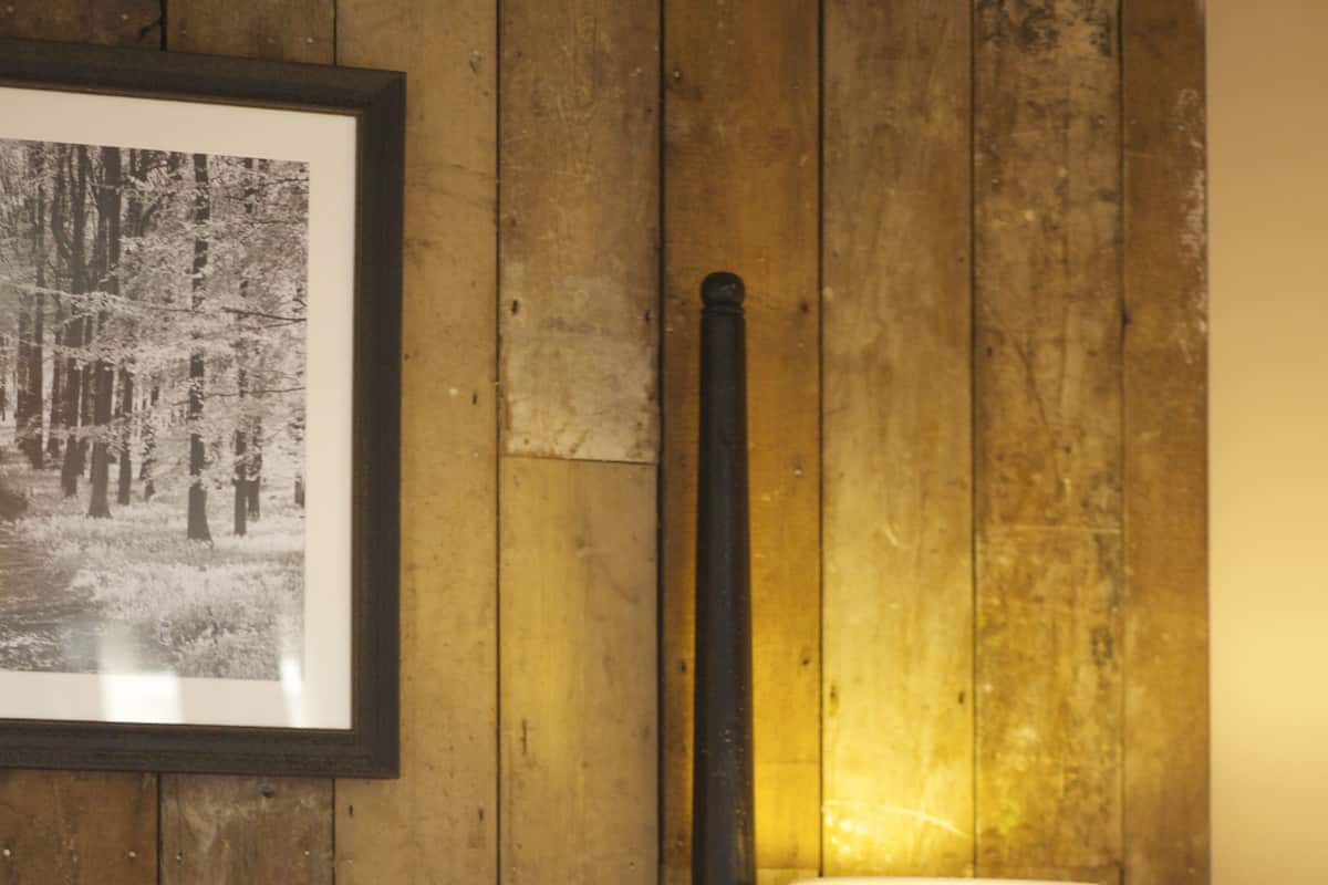 Uma cama com almofadas listradas, um quadro na parede, uma luminária e um telefone em uma mesa de cabeceira de madeira.