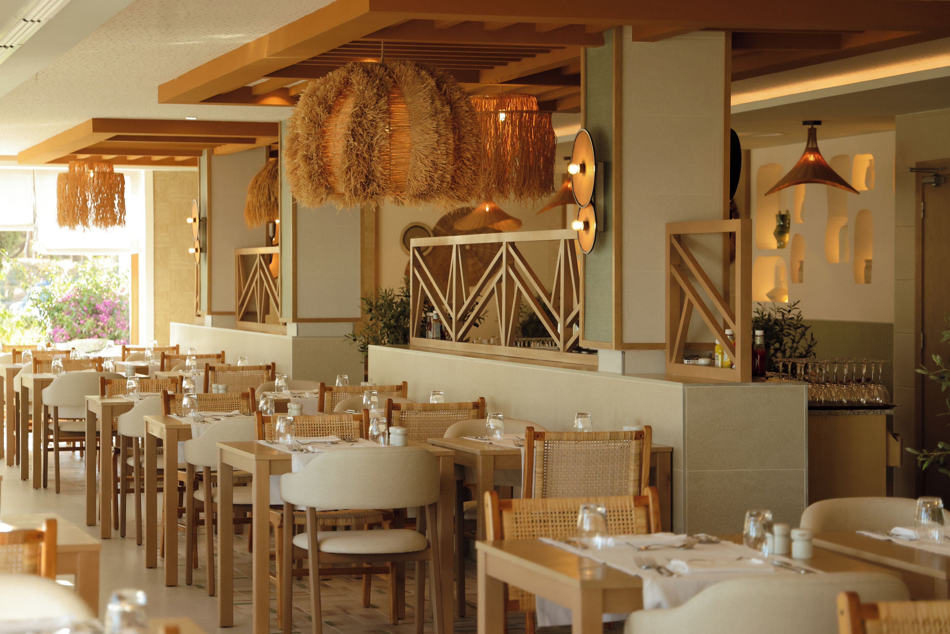 Um restaurante com mesas e cadeiras de madeira, decorações penduradas e um espaço de bar com copos.