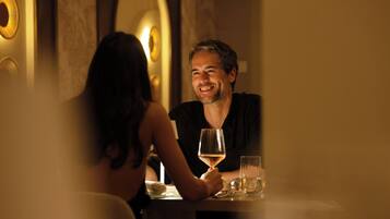 Um casal sentado à mesa em um quarto com iluminação acolhedora, parede decorativa e um candelabro.