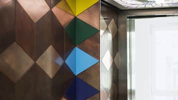 Interior moderno com paredes de padrão geométrico, porta de vidro e teto com design em vitrais.