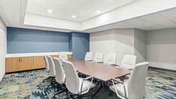 Sala de conferências com uma mesa comprida, cadeiras brancas, parede azul decorativa e carpete estampado.
