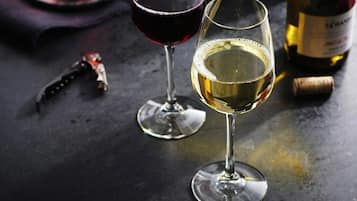 Duas taças de vinho sobre uma superfície escura, uma com vinho tinto e outra com vinho branco, e uma garrafa de vinho ao fundo.