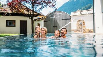 Uma piscina com pessoas, rodeada por edifícios e uma montanha ao fundo.