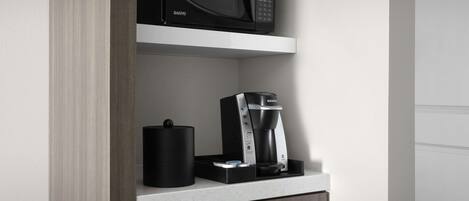 Cozinha com micro-ondas, cafeteira e um recipiente preto sobre uma bancada branca.