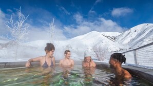 Um grupo de pessoas em uma nascente termal, cercadas por montanhas cobertas de neve.