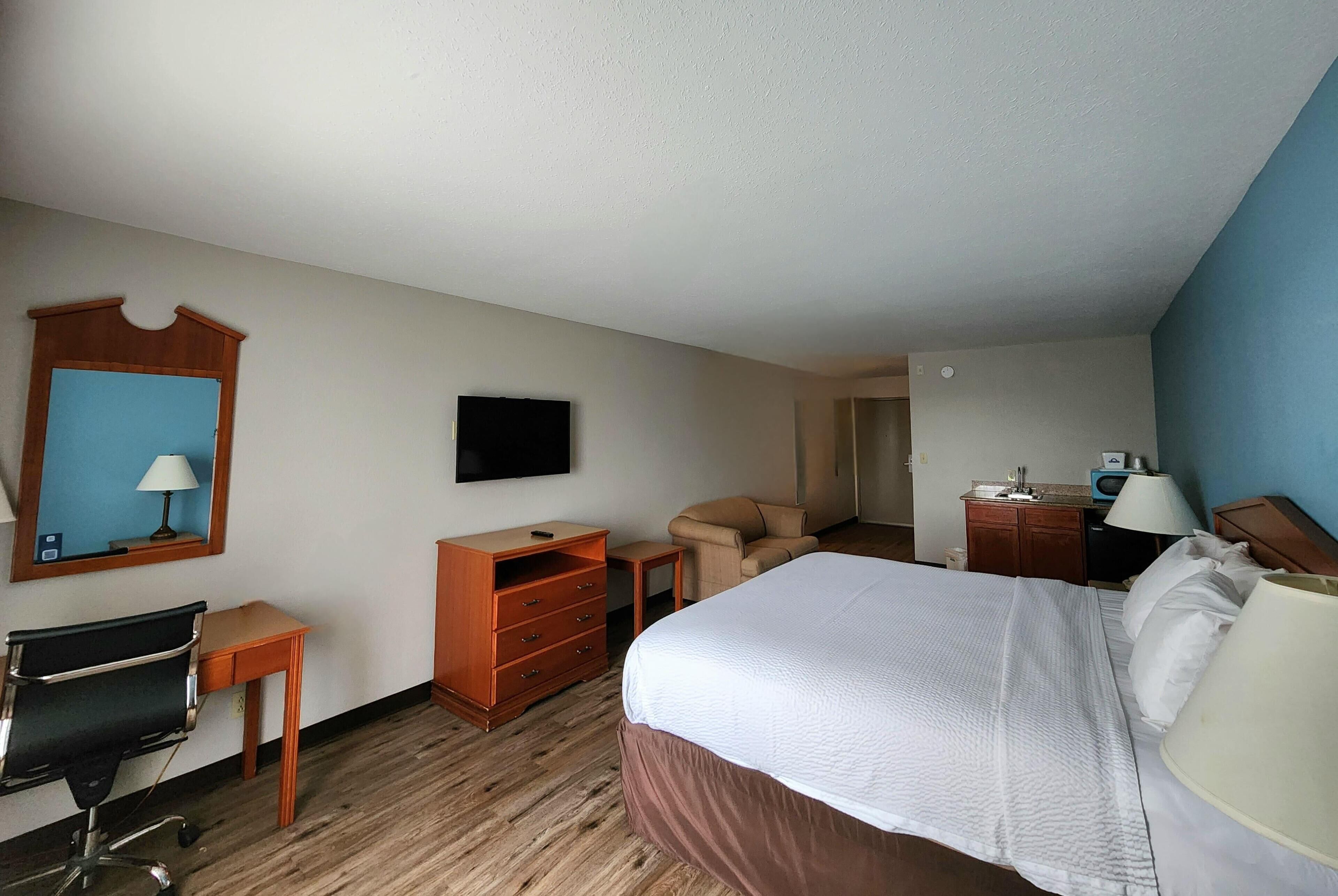 Quarto de hotel com cama, escrivaninha, cadeira, penteadeira, televisão e banheiro.