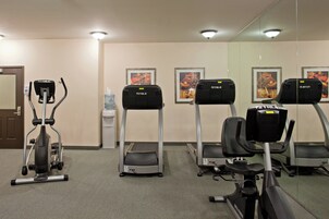 Sala de ginástica com esteiras, elíptico e bebedouro.