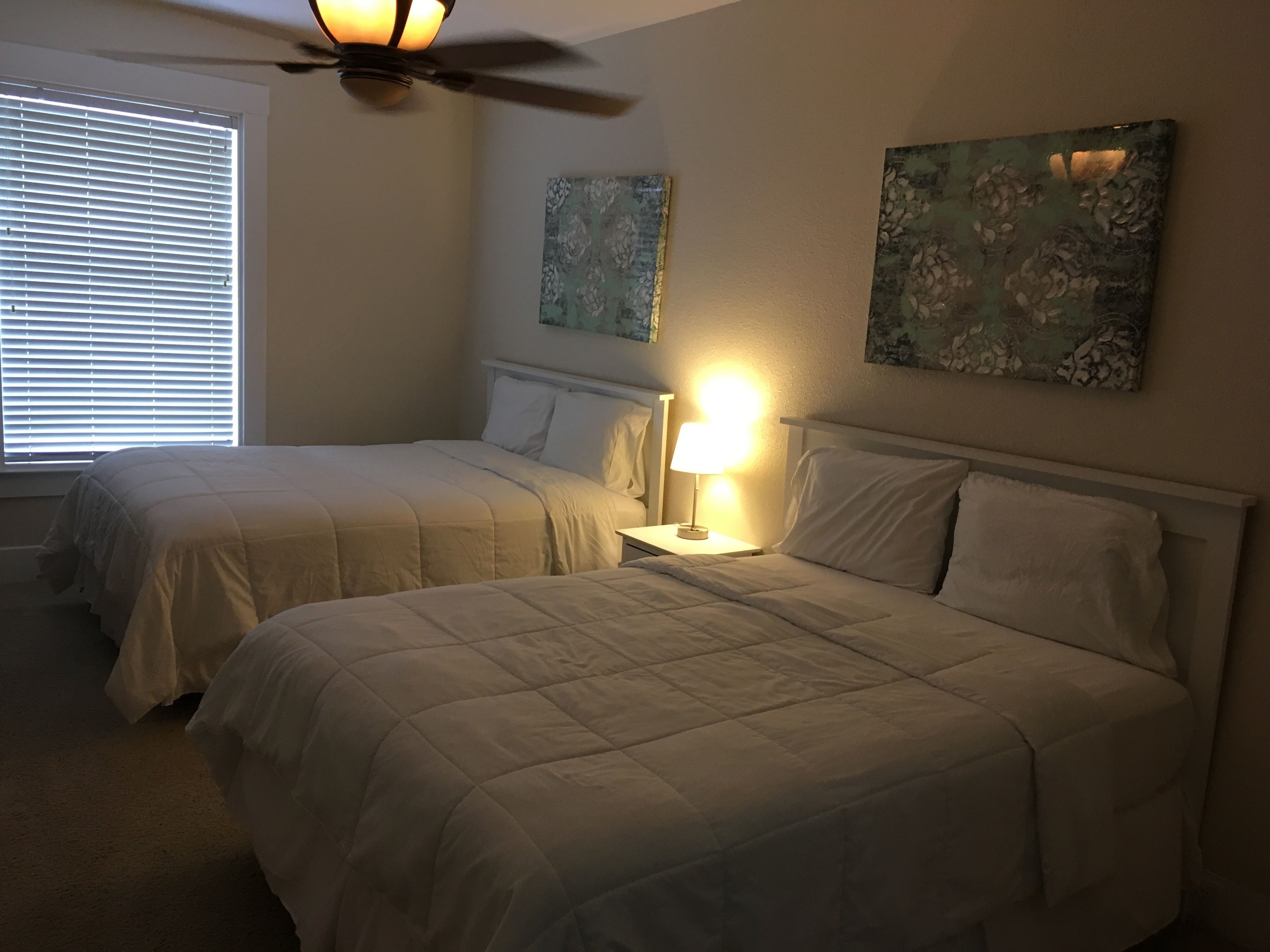 Quarto com duas camas, um ventilador de teto e obras de arte nas paredes.