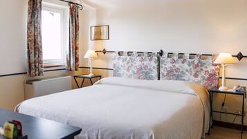 Quarto de hotel bem arrumado com uma cama grande, duas mesas de cabeceira com luminárias, uma janela com cortinas florais e um quadro pendurado na parede.