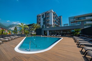Um hotel moderno com piscina no terraço, espreguiçadeiras e vista para as montanhas.